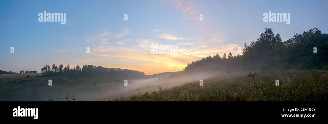 Beautiful summer hazy landscape with foggy hollow and green hills ...