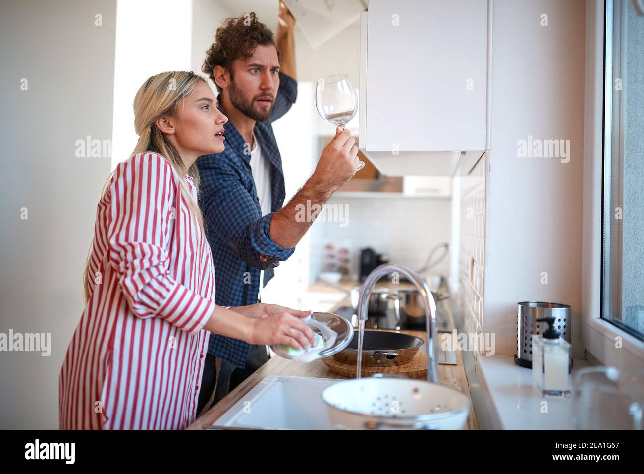 A young couple washing and checking cleanliness of the dishes in a ...