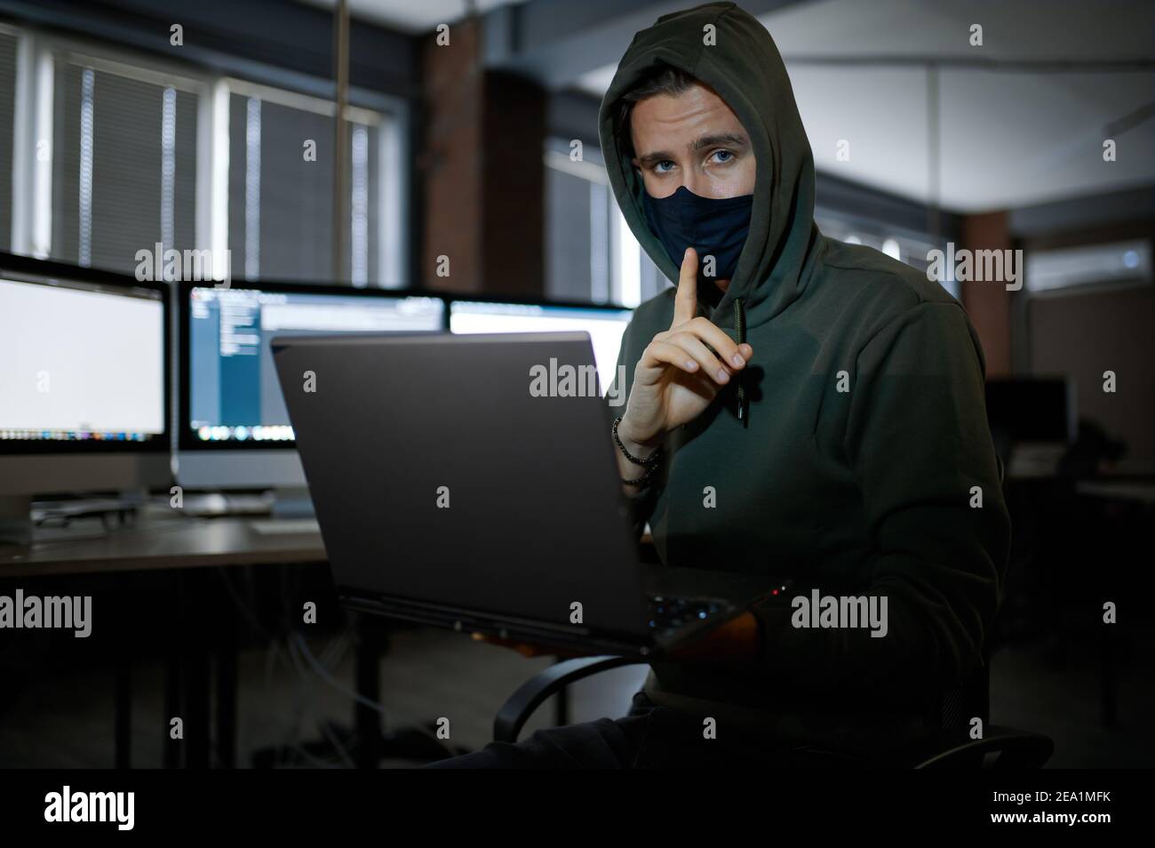 Male hacker in hood works on laptop in dark office Stock Photo - Alamy