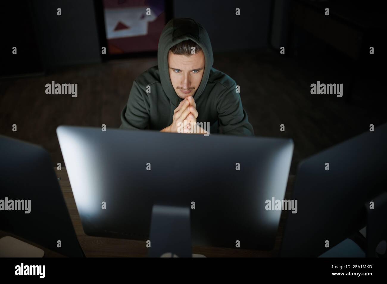 Serious male hacker in hood works on computer Stock Photo - Alamy