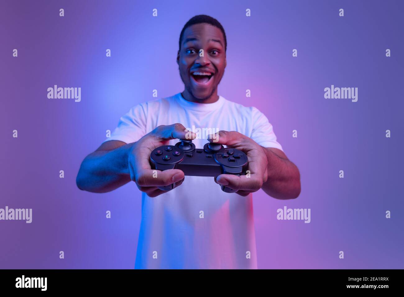 Excited african american guy playing video games with joystick in neon ...