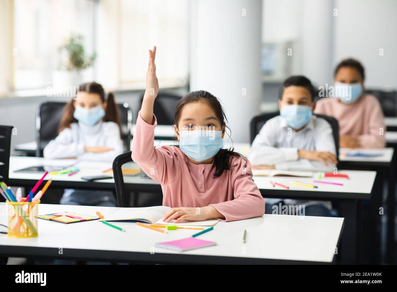 Children raising hands at classroom, wearing medical mask Stock Photo ...
