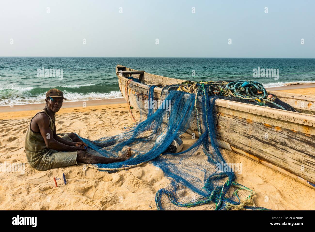 Man fixing his nets in his fishing boats on a beach in Robertsport ...
