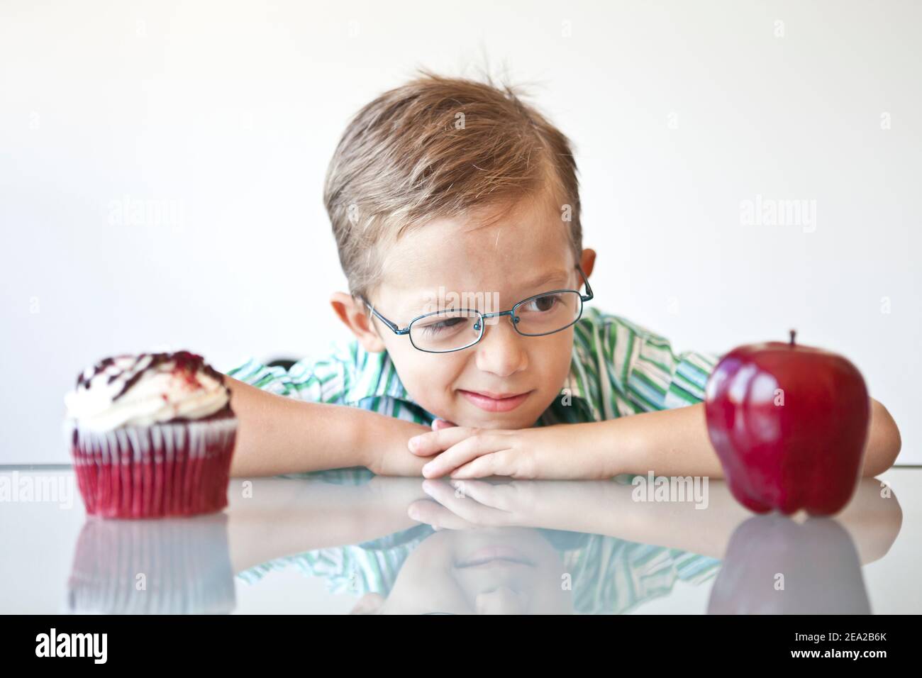 A cute little boy with eyeglasses choosing between healthy and ...