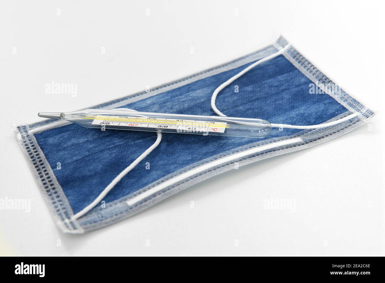 Blue medical mask and medical mercury-in-glass thermometer on white ...