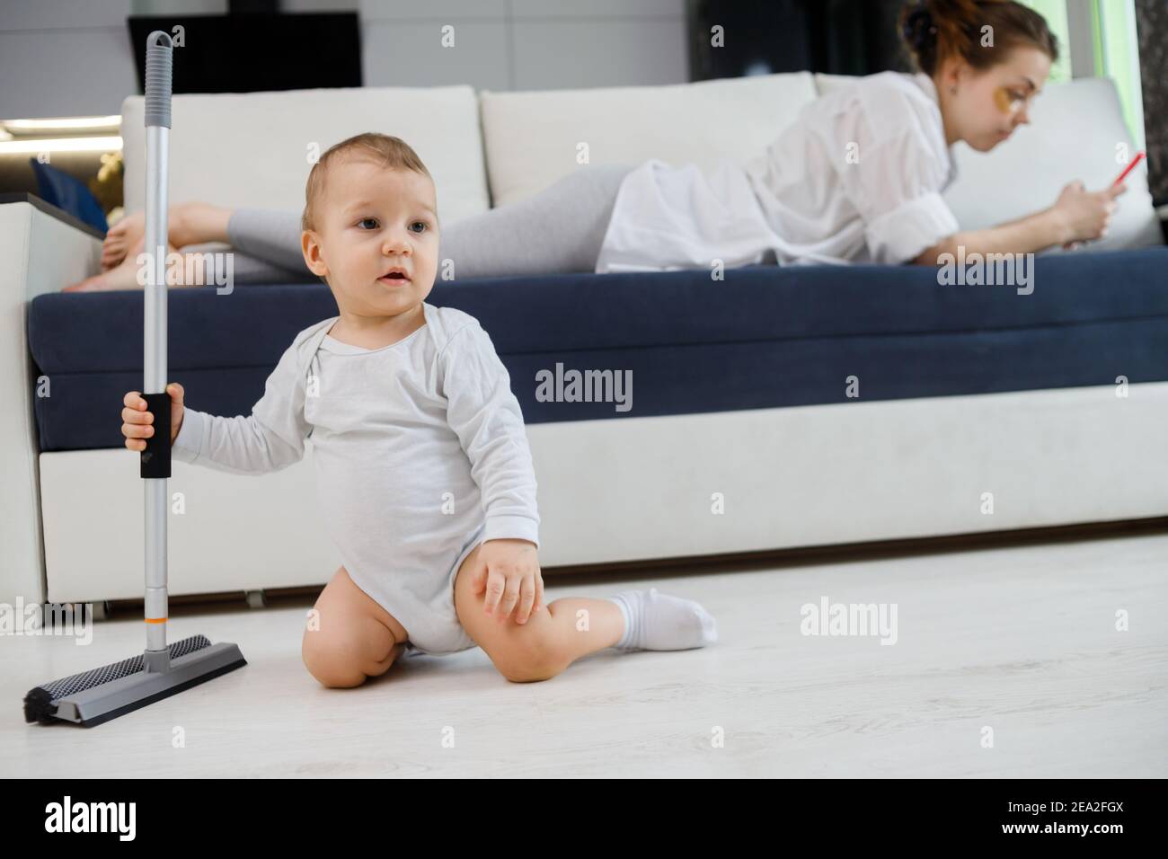 Baby boy play with mop, while mother surfing in your smartphone lying ...