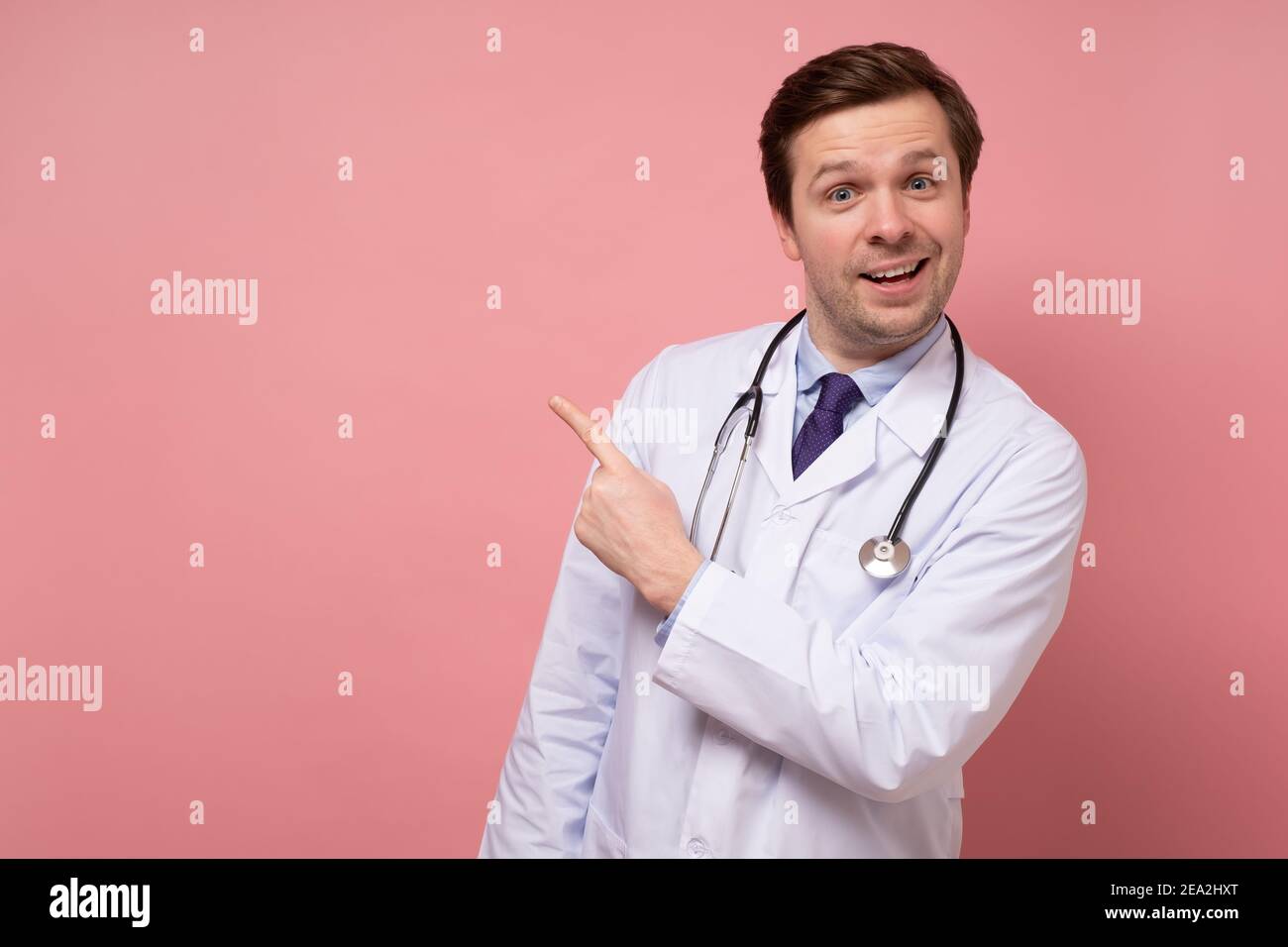 Male doctor makes a pointing finger gesture, isolated over a pink ...