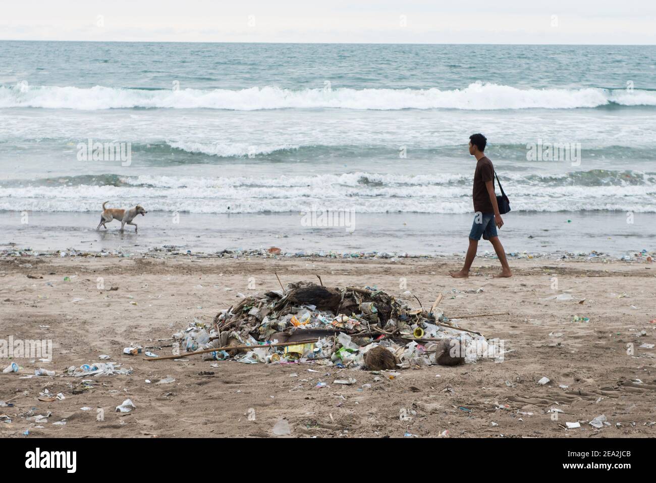 A tourist walks along a beach in Bali covered in piles of plastic and ...