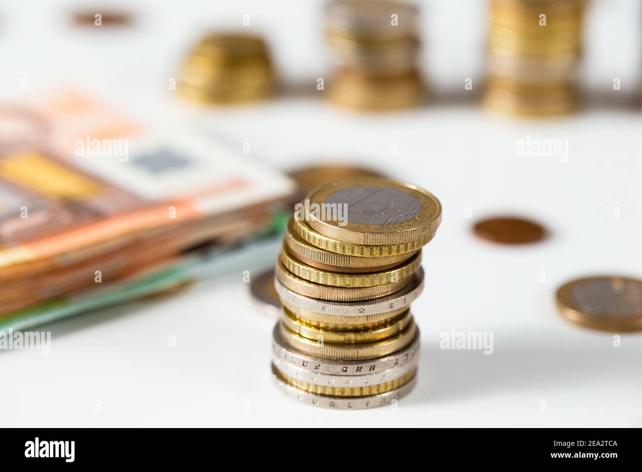Euro coins standing in column on white table with heap of banknotes in ...