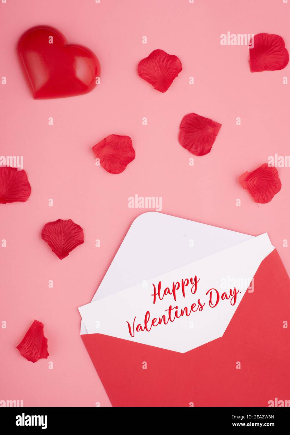open envelope with card, heart and rose petals on pink background with ...