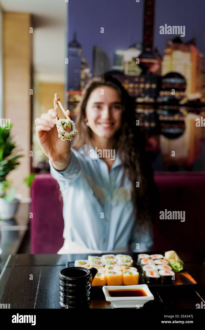 Happy girl is giving sushi to you in japanese restaurant. Young girl is ...