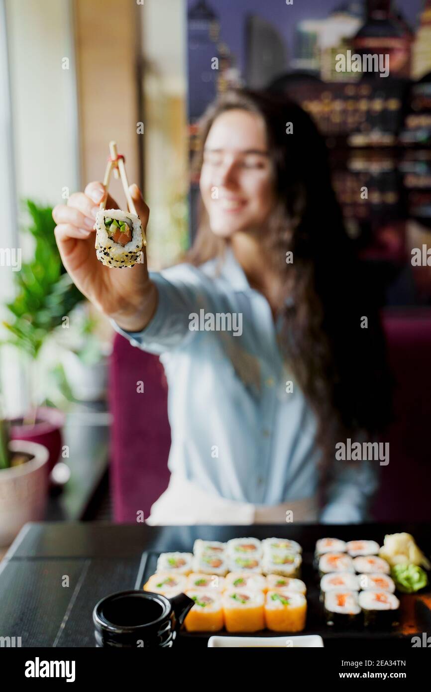 Happy girl is giving sushi to you in japanese restaurant. Young girl is ...
