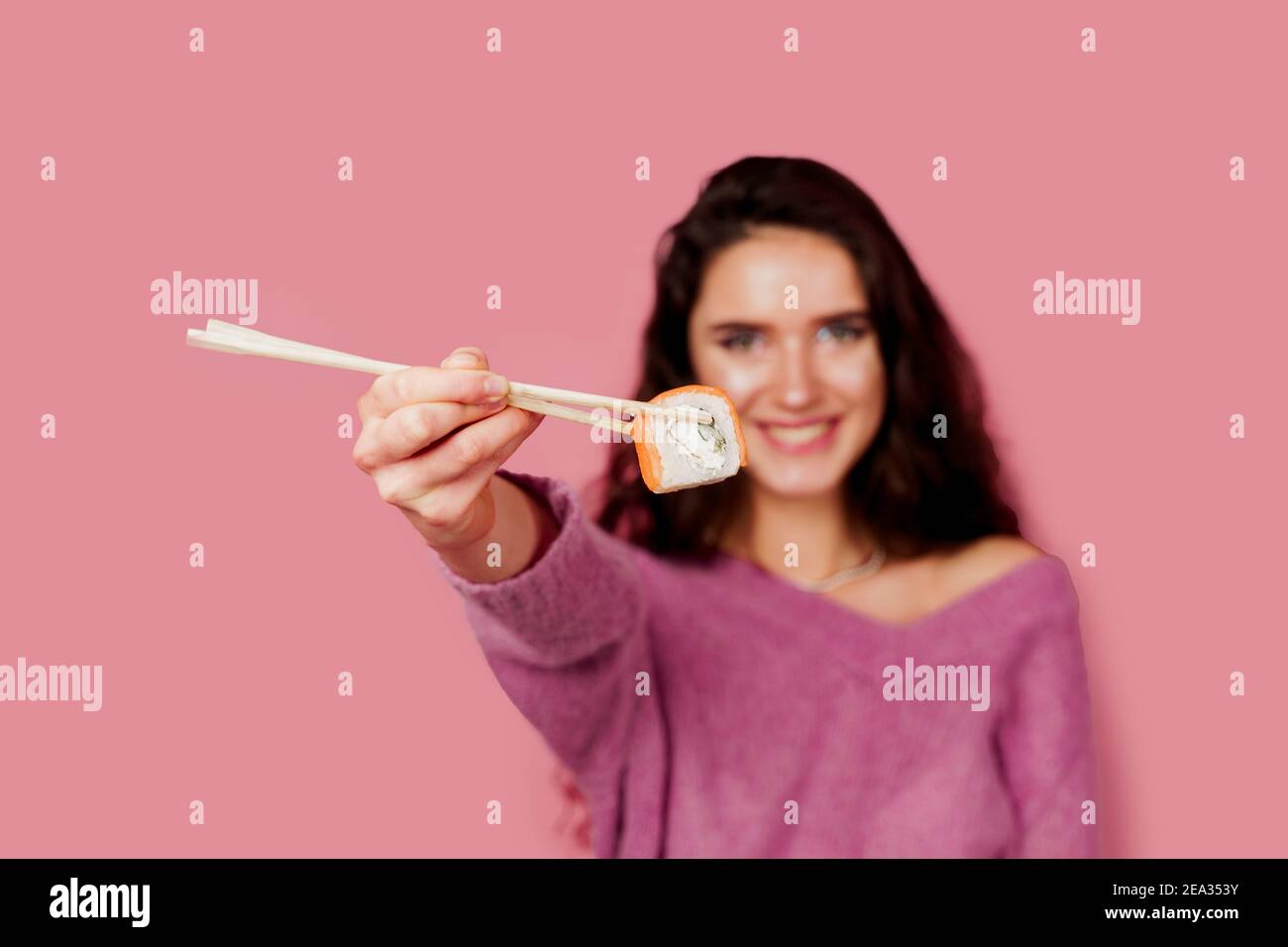 Happy girl giving sushi to you isolated on pink background. Young girl ...