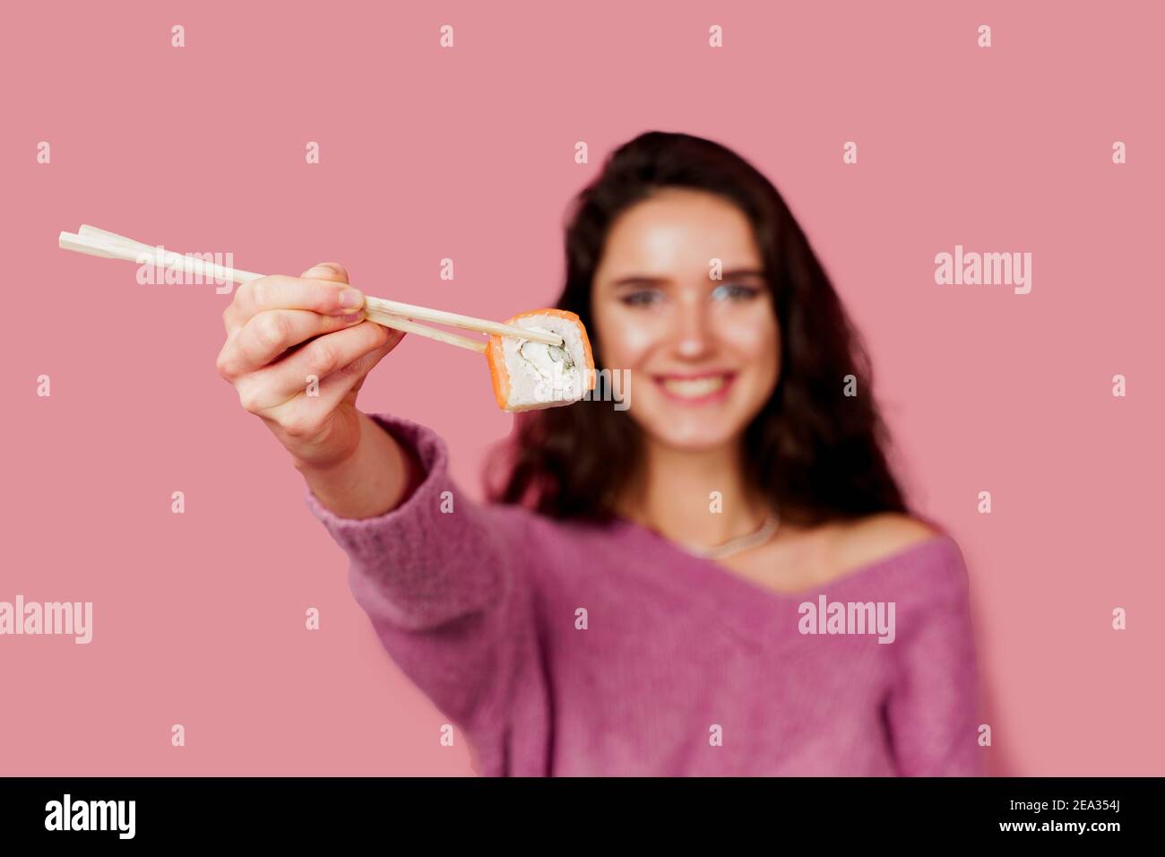 Happy girl giving sushi to you isolated on pink background. Young girl ...