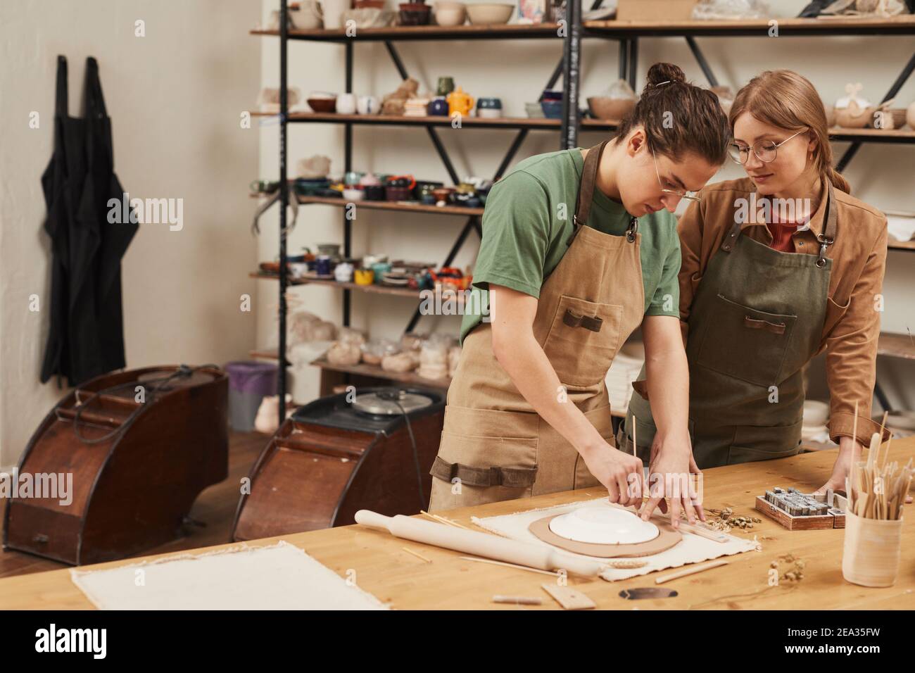 Warm toned portrait of two young people making ceramics while working ...