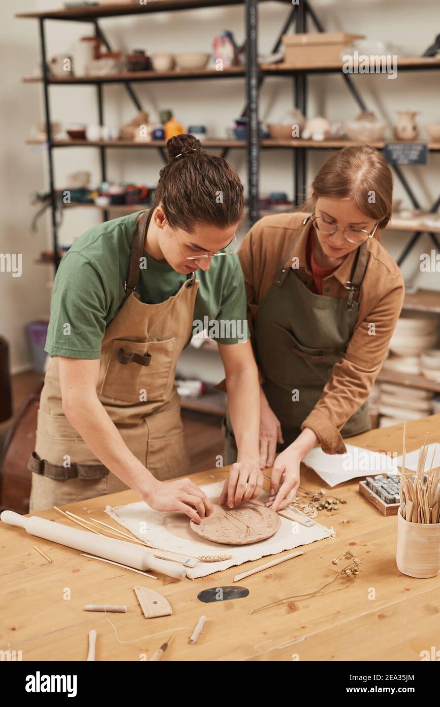 Vertical warm toned portrait of two young people making ceramics while ...