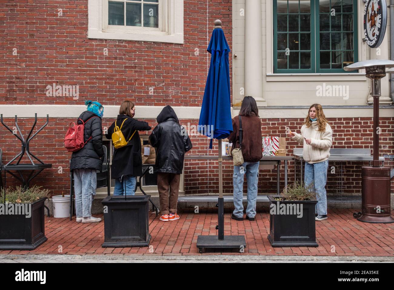 Young women line up to pick up takeout or take away orders outside of a ...