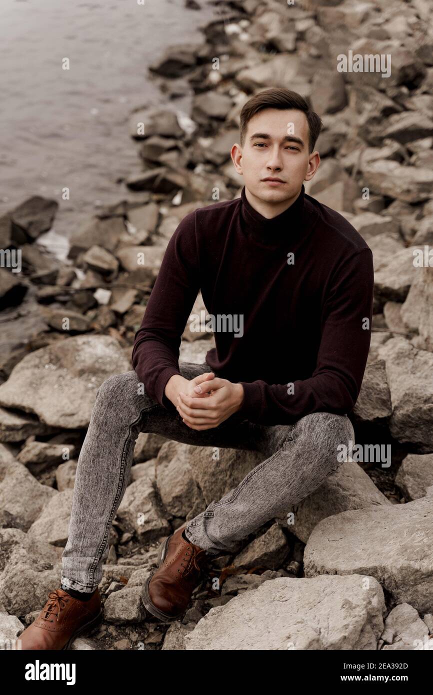 Handsome man seats on the rocks near lake. Professional male model ...