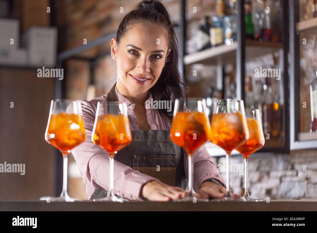 Barmaid offers aperol spritz cocktails on a bar smiling at the camera ...