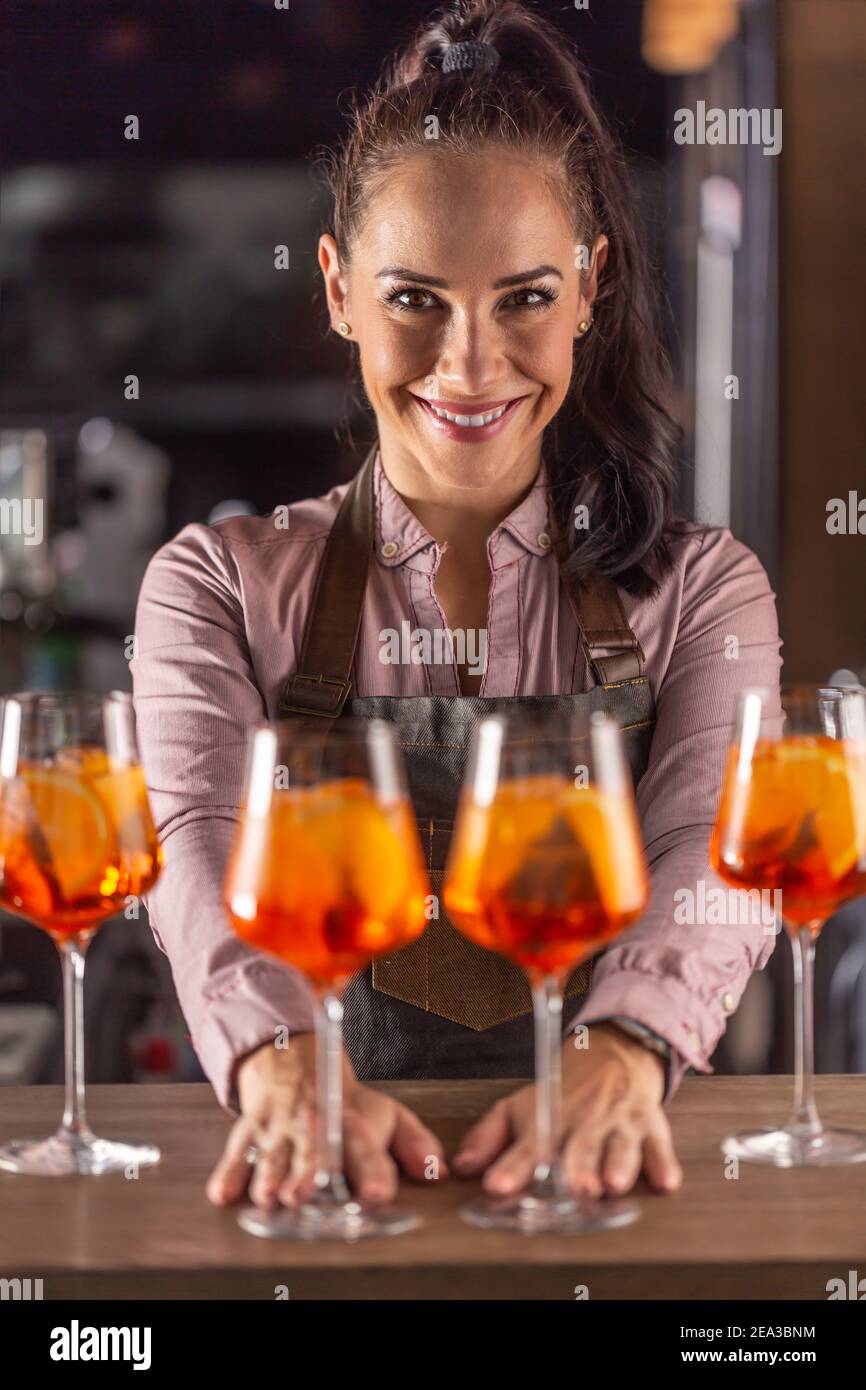 Barmaid offers aperol spritz cocktails on a bar smiling at the camera ...