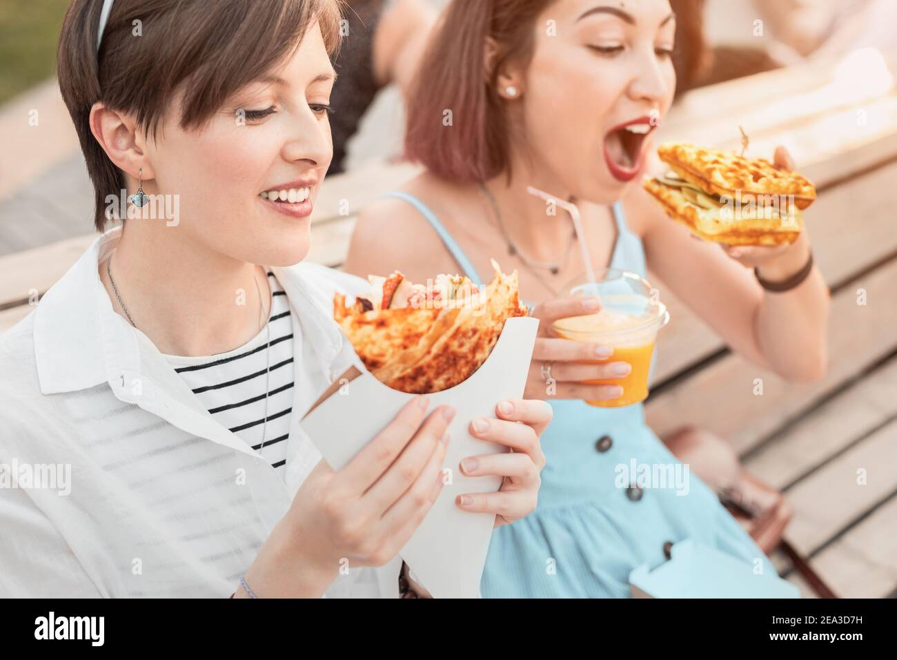 Two happy women friends relaxing in city park and eating modern street ...
