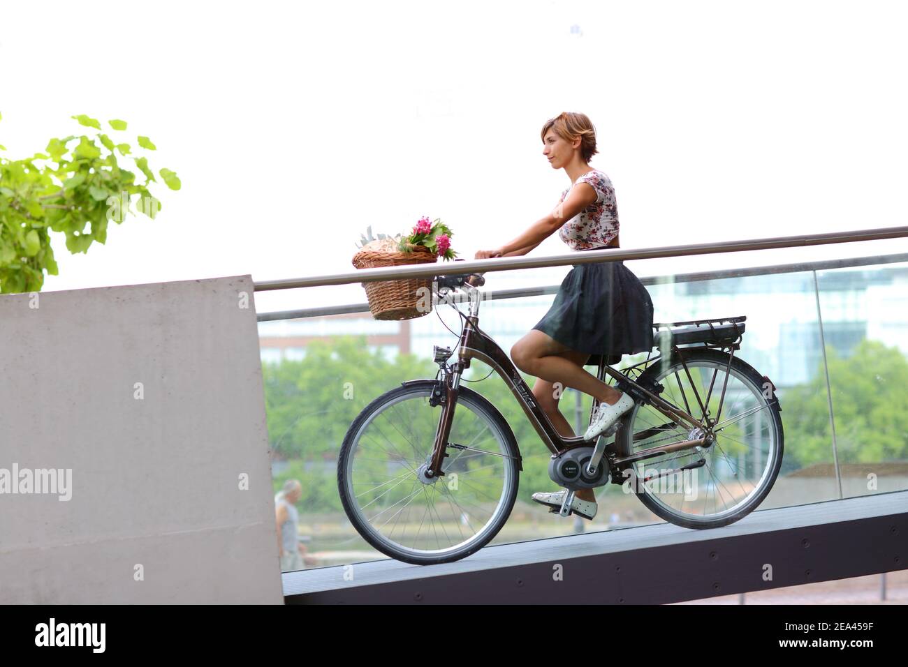 Young woman in short dress rides an electric e-bike with basket and ...
