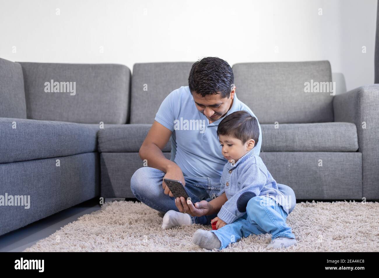Mexican father and son looking at the phone on the carpet at home Stock ...