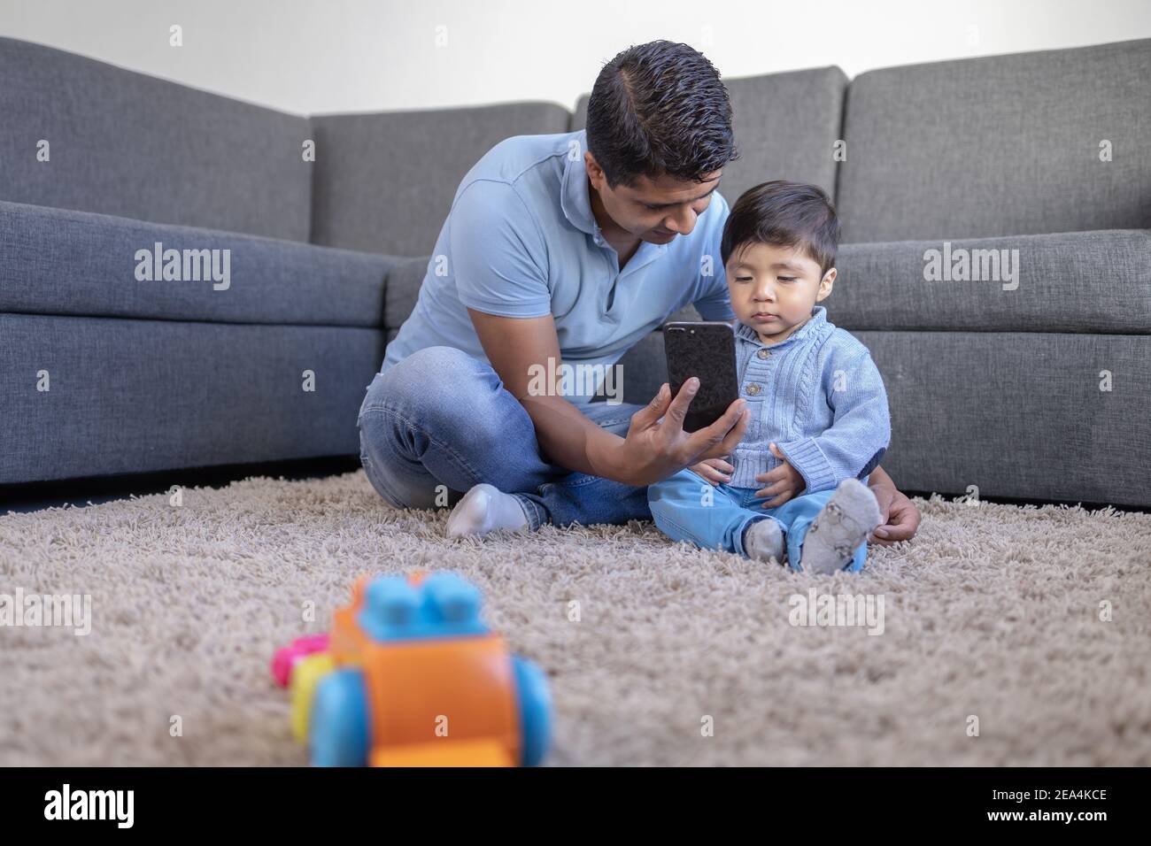 Mexican father and son looking at the phone on the carpet at home Stock ...
