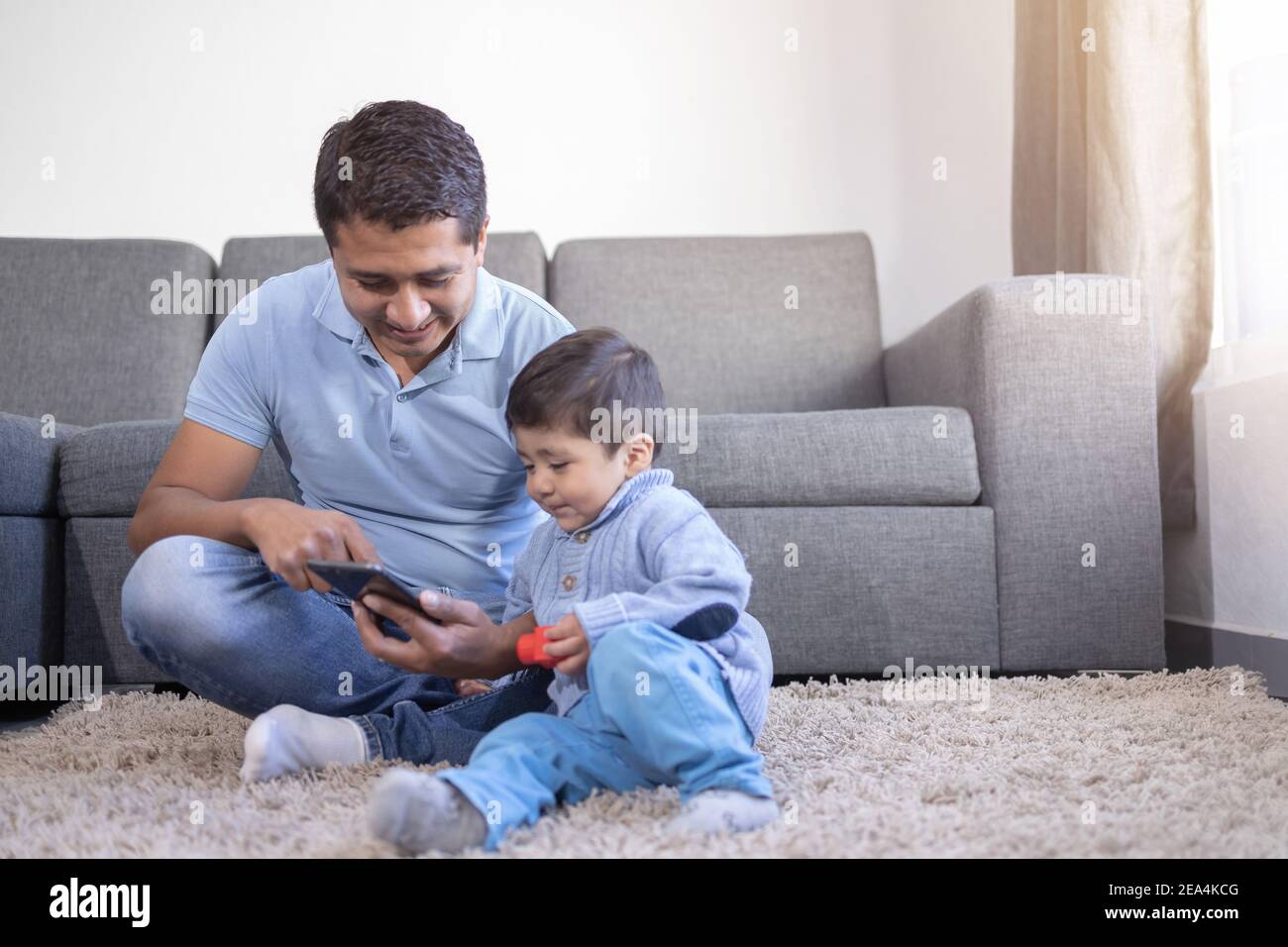 Mexican father and son looking at the phone on the carpet at home Stock ...
