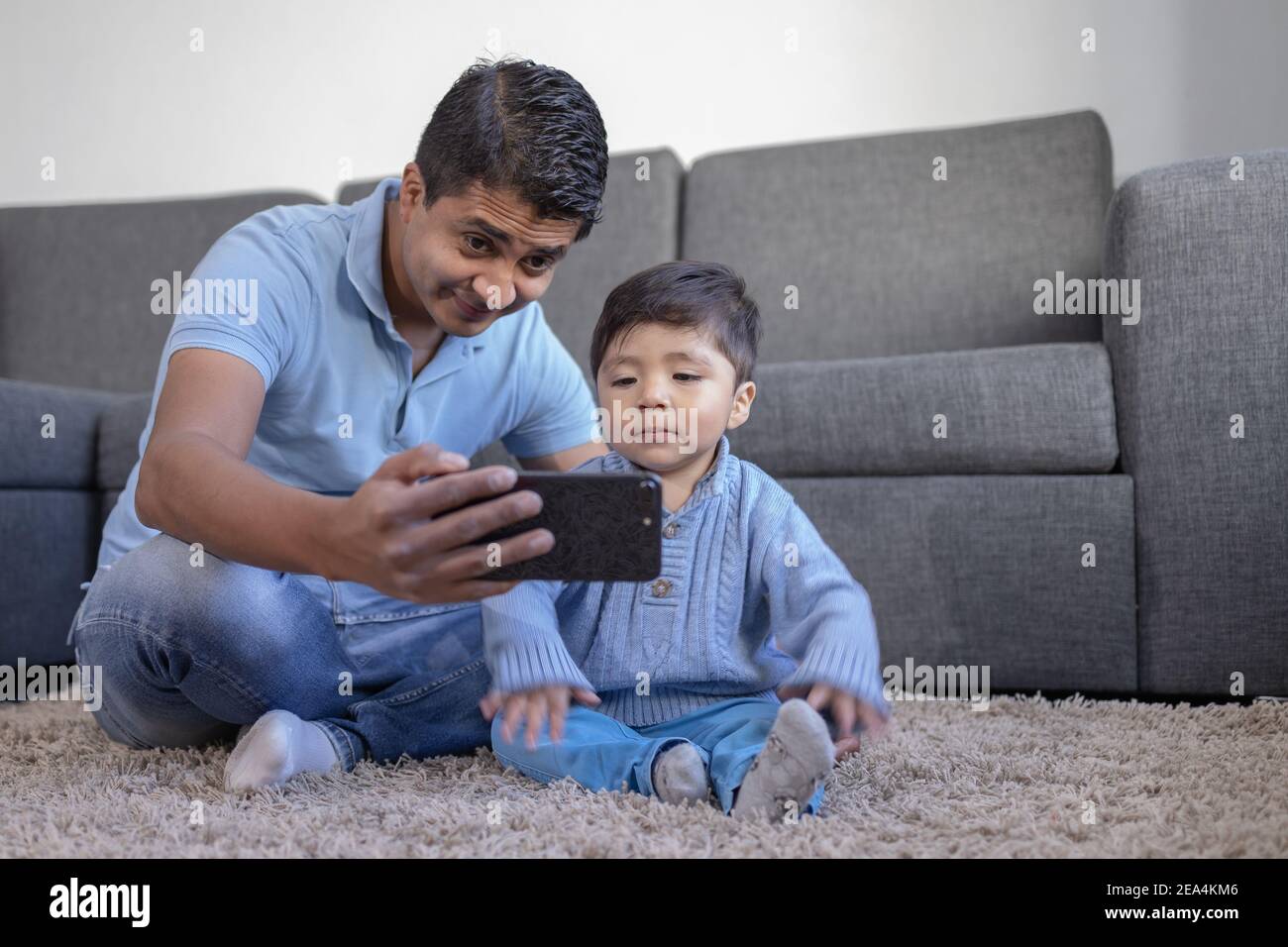 Mexican father and son looking at the phone on the carpet at home Stock ...
