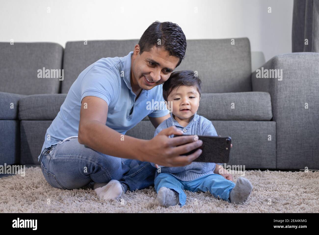 Mexican father and son looking at the phone on the carpet at home Stock ...