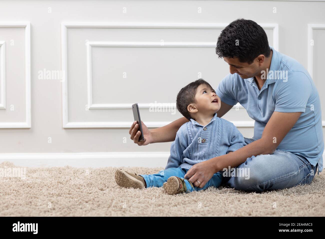 Mexican father and son looking at the phone on the carpet at home Stock ...