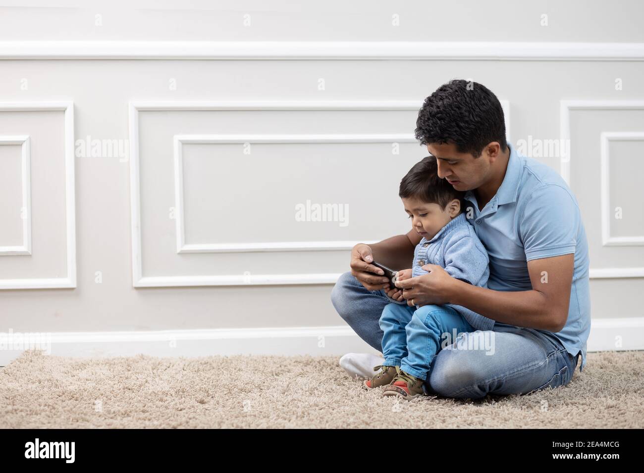 Mexican father and son looking at the phone on the carpet at home Stock ...