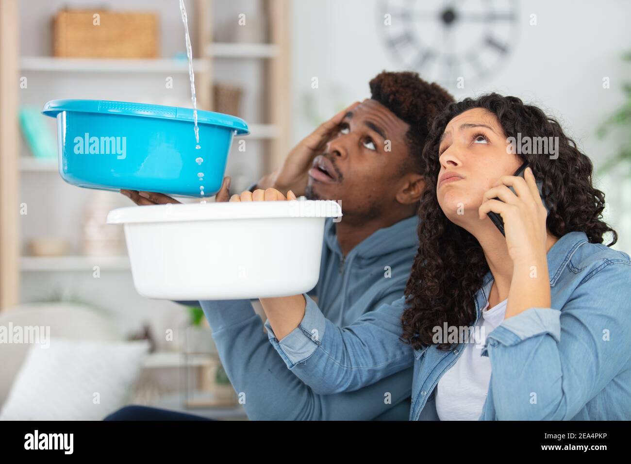 husband and wife with bucket collecting water from damaged ceiling ...