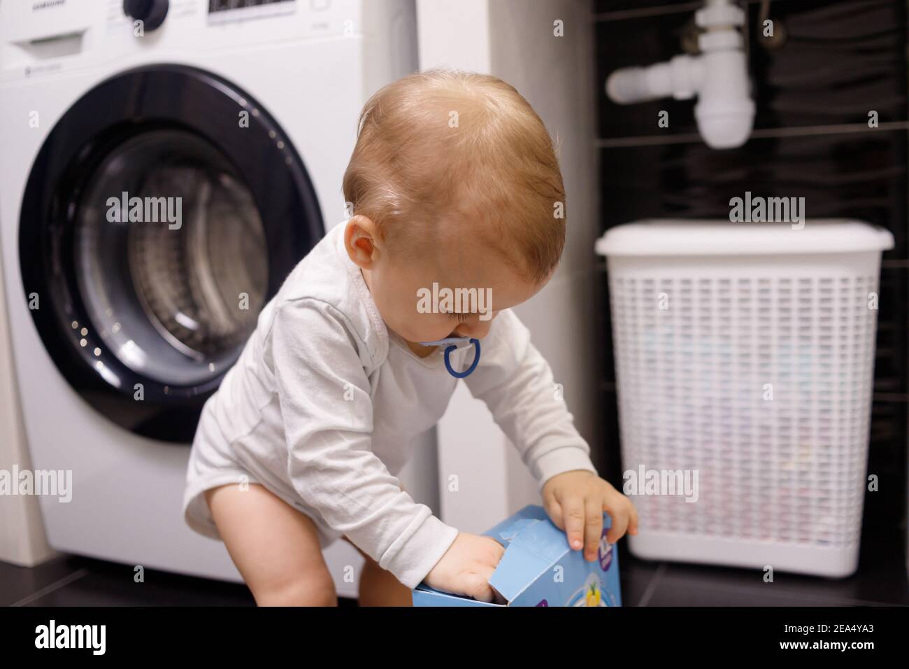 Infant boy open box with tablet for dishwasher or detergent in bathroom ...