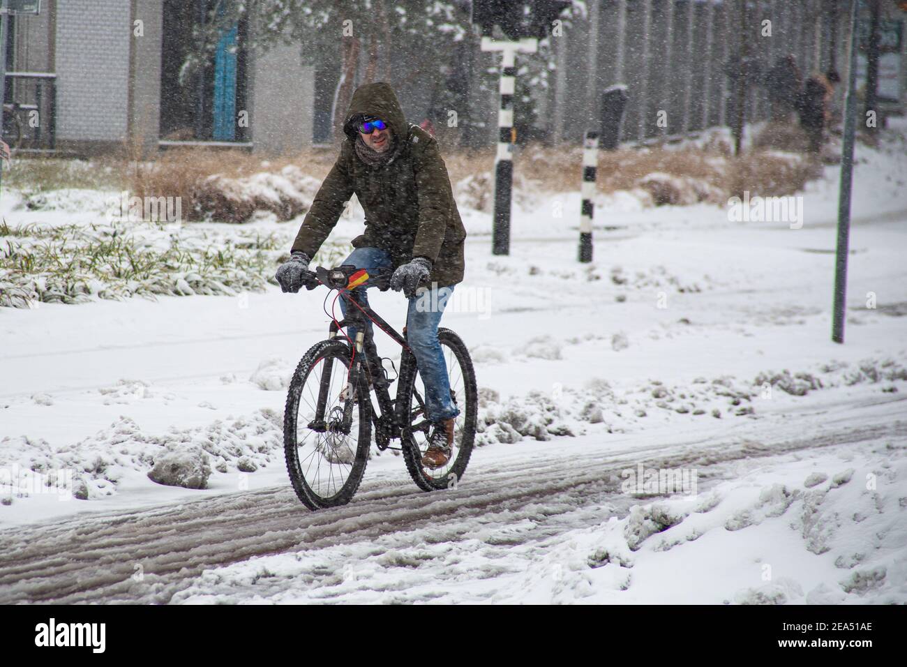 A man cycling a bike on the snow covered bicycle lane. Blizzard from ...