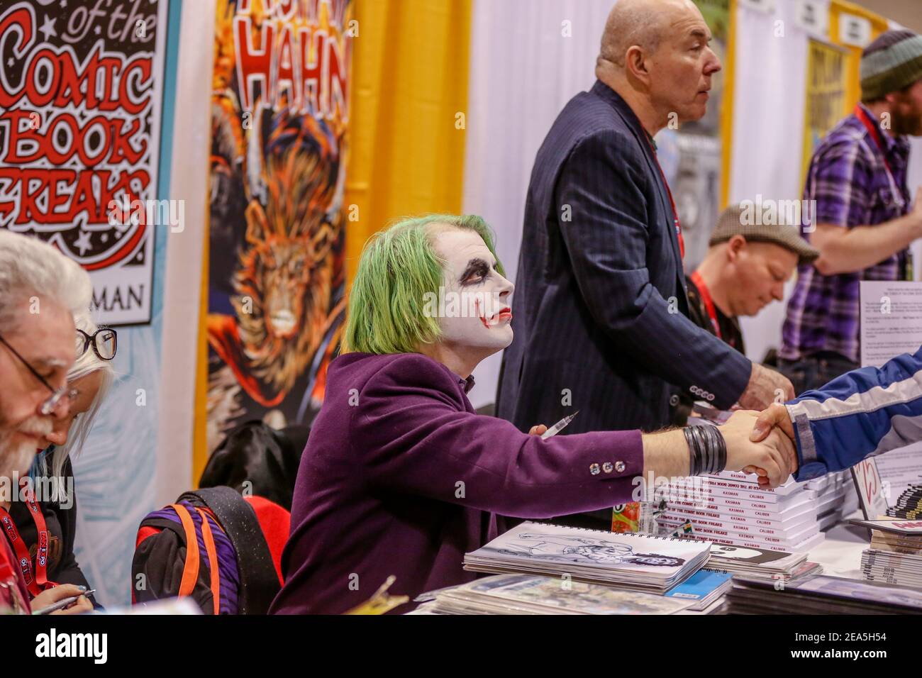 A person dressed as DC Comic character The Joker sits behind the table ...