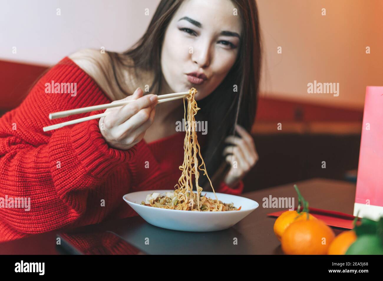 Beautiful smiling young asian woman in red clothes eating noodles with ...