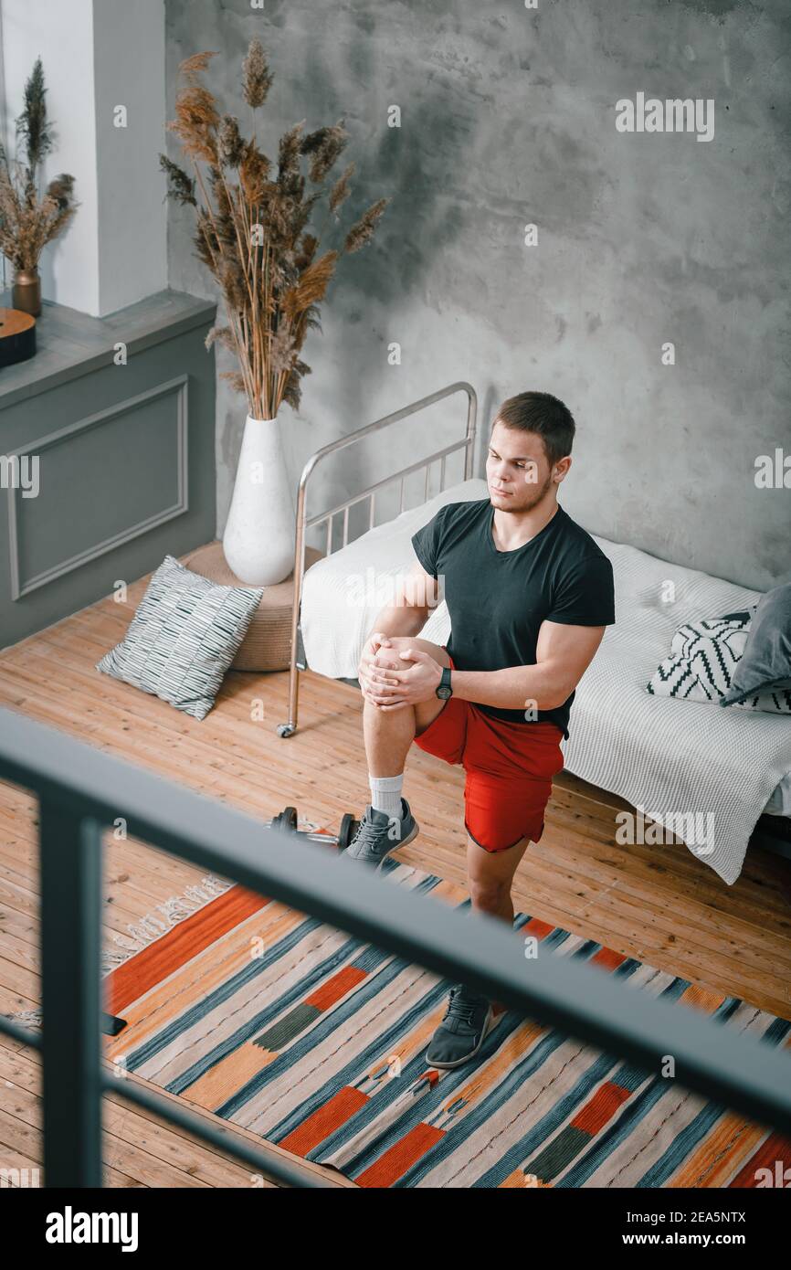 A cheerful athlete with black hair lunges, stretching in the bedroom ...