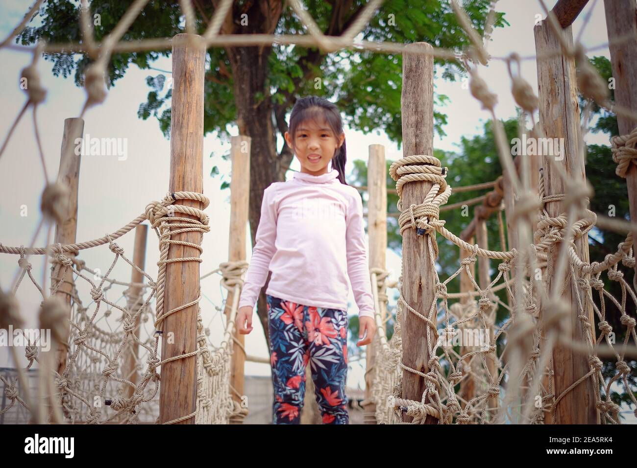 A cute young Asian girl running along a bridge in a playground obstacle ...