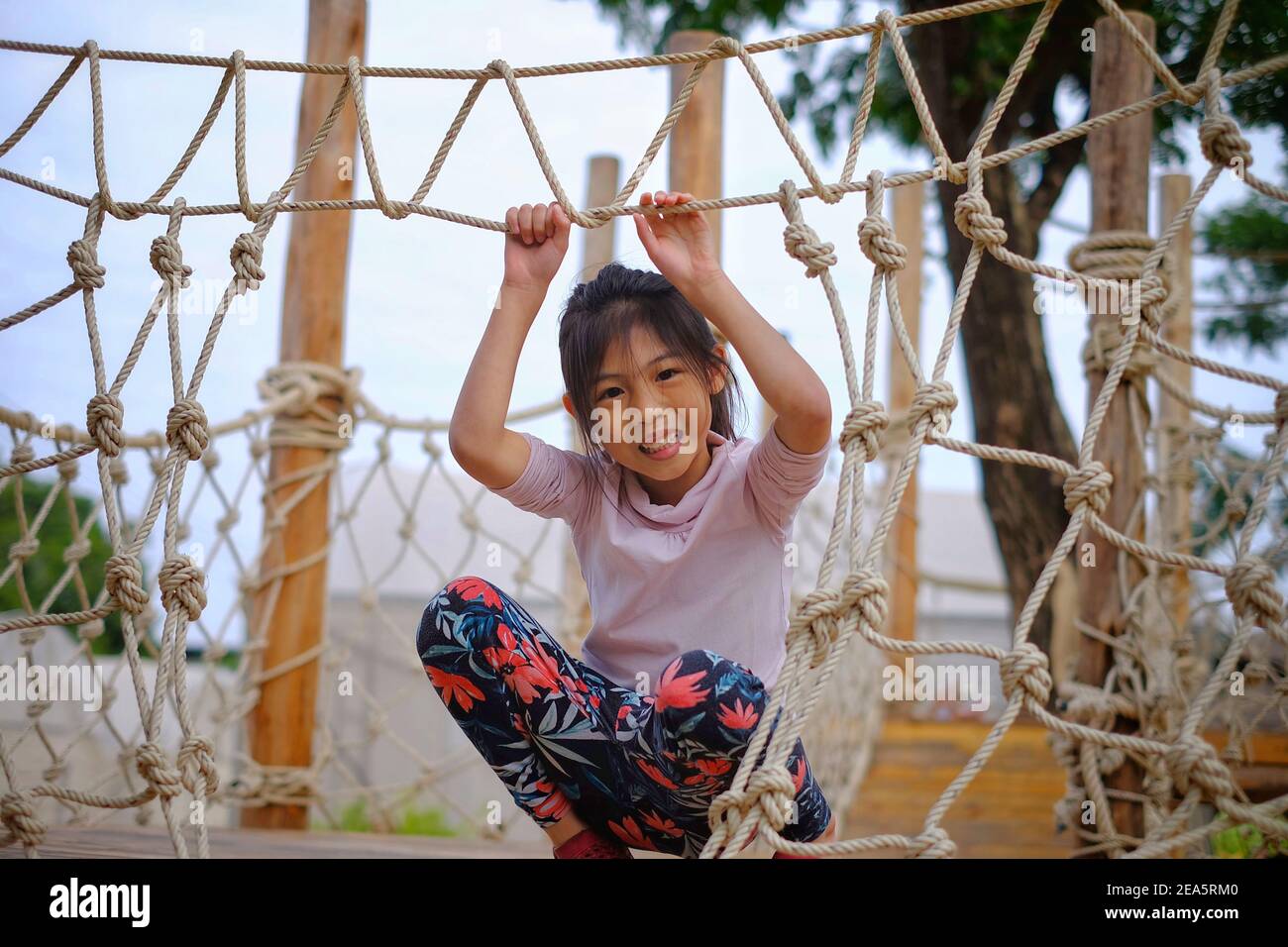 A cute young Asian girl running along a bridge in a playground obstacle ...