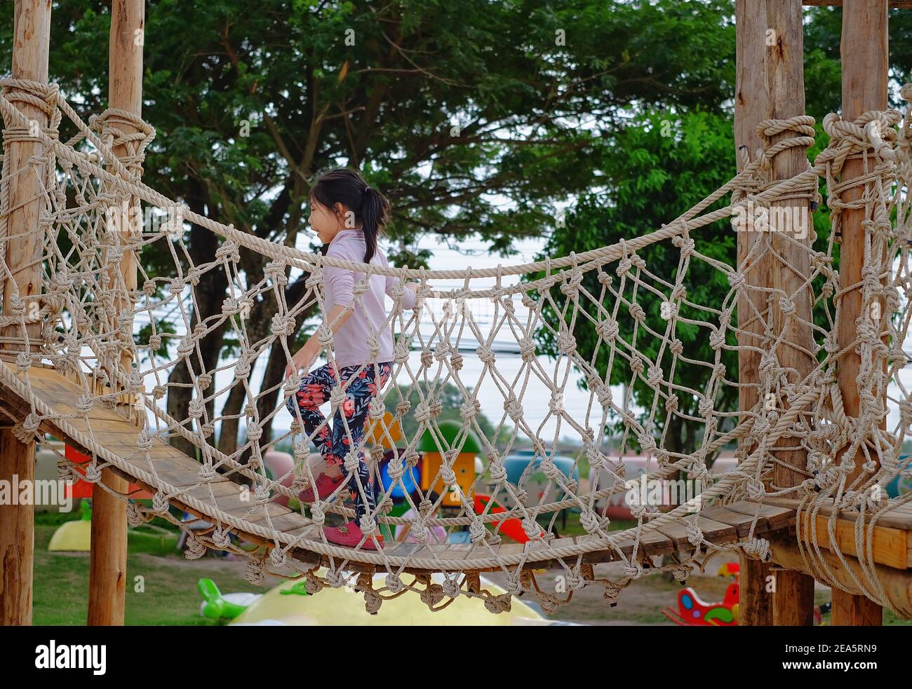 A cute young Asian girl running along a bridge in a playground obstacle ...