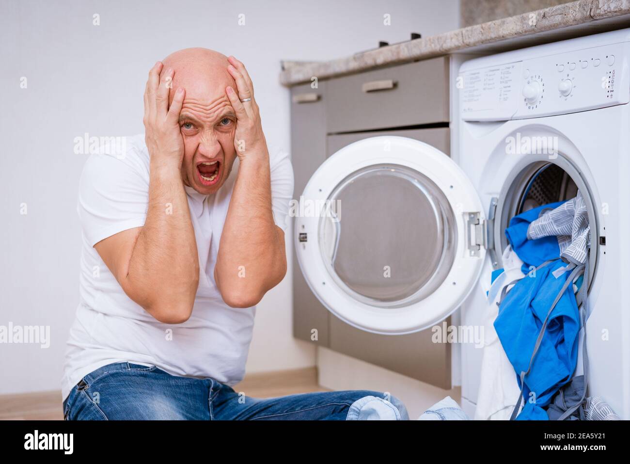 tired bald man sitting with dirty laundry in the washing machine ...