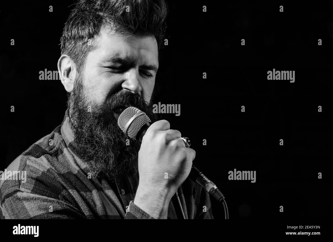 Man with tense face holds microphone, singing song, black background ...