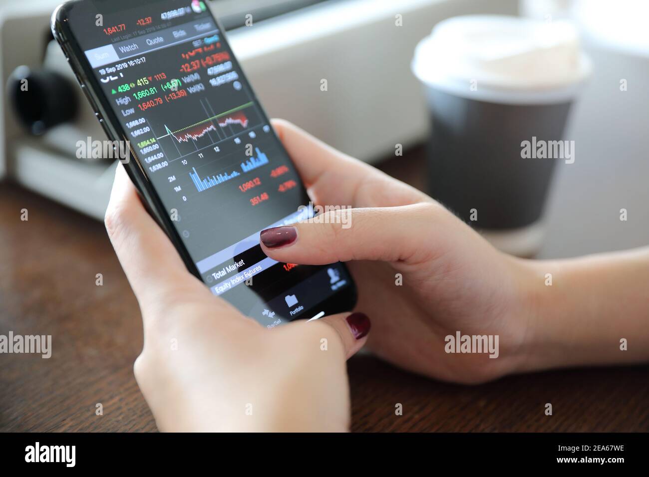 Female hand with smartphone trading stock online in coffee shop ...