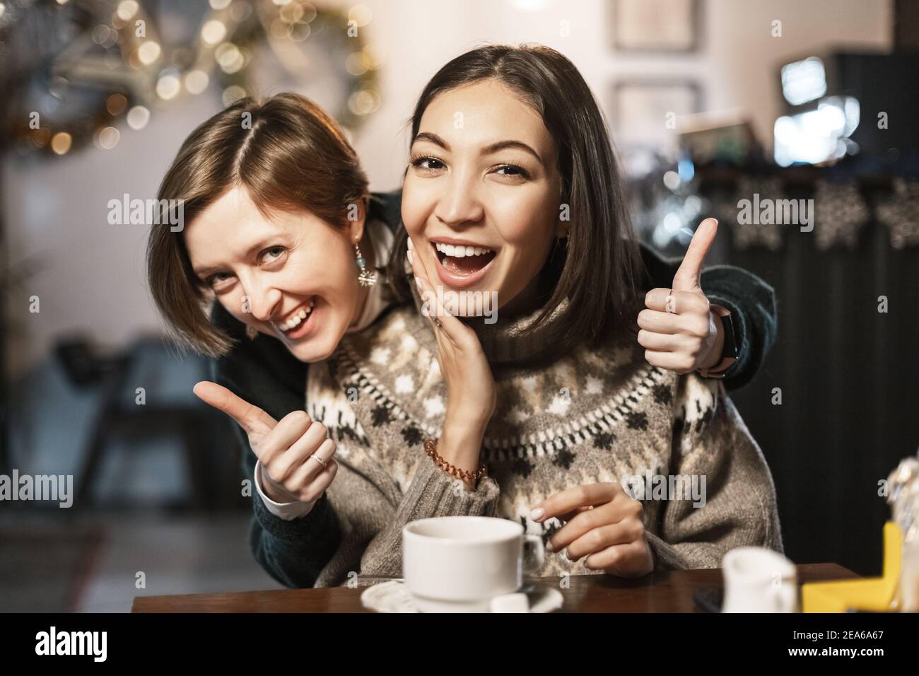 Two female friends hug and have fun sitting in a cafe at the christmas ...