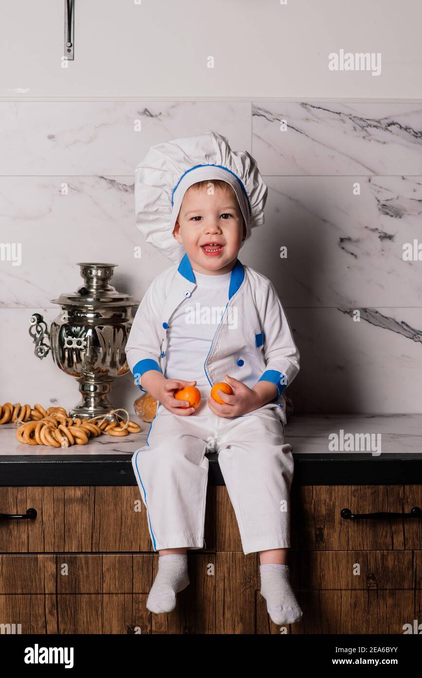 Little cute cook with cutlery sitting on kitchen, twin brothers ...