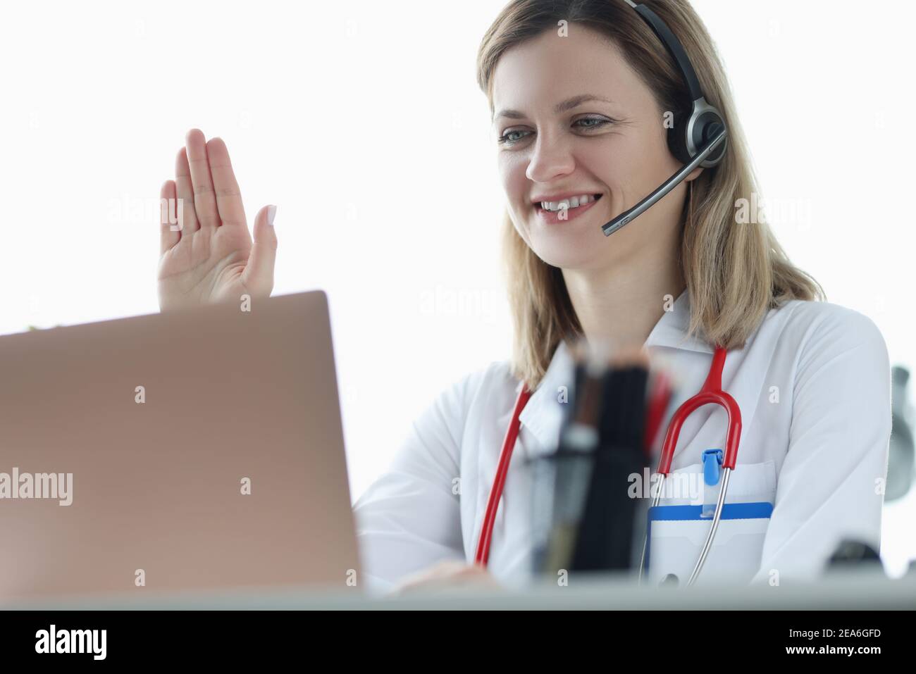 Doctor in headphones with microphone waving his hand at laptop screen ...