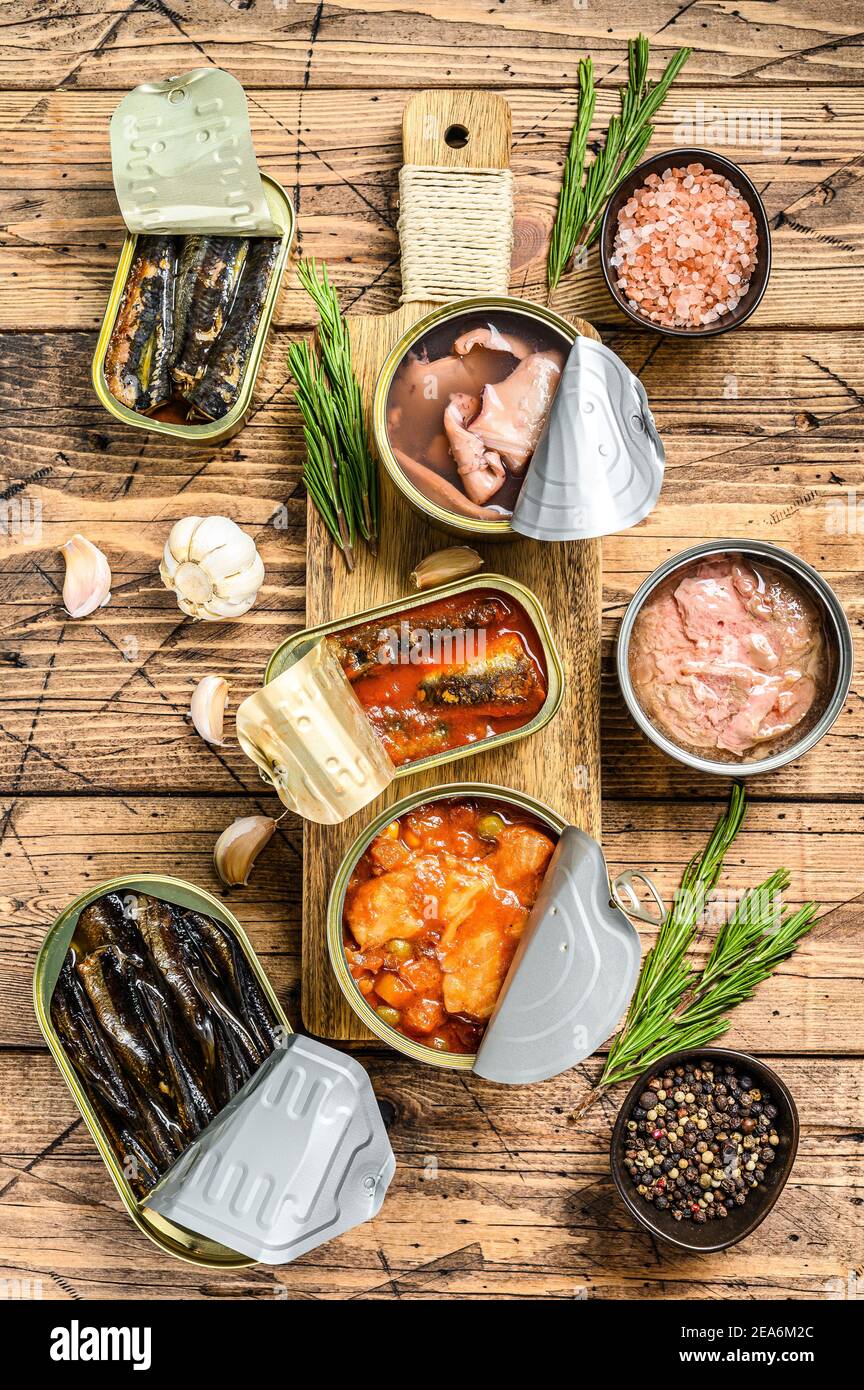 Various canned fish and seafood in a metal cans. Wooden background. Top ...