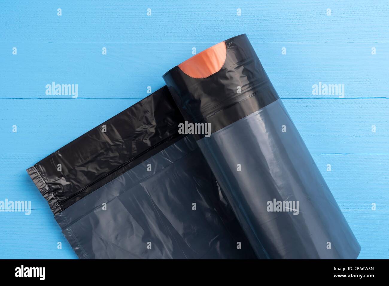 Black garbage bags on a roll. Wooden blue background. Orange strap ...